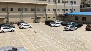 Um parque de estacionamento com vários carros estacionados em frente a um edifício com vários andares e unidades de ar condicionado na fachada.