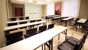 Uma sala de conferência com várias mesas e cadeiras, uma janela grande com cortinas e uma porta ao fundo.