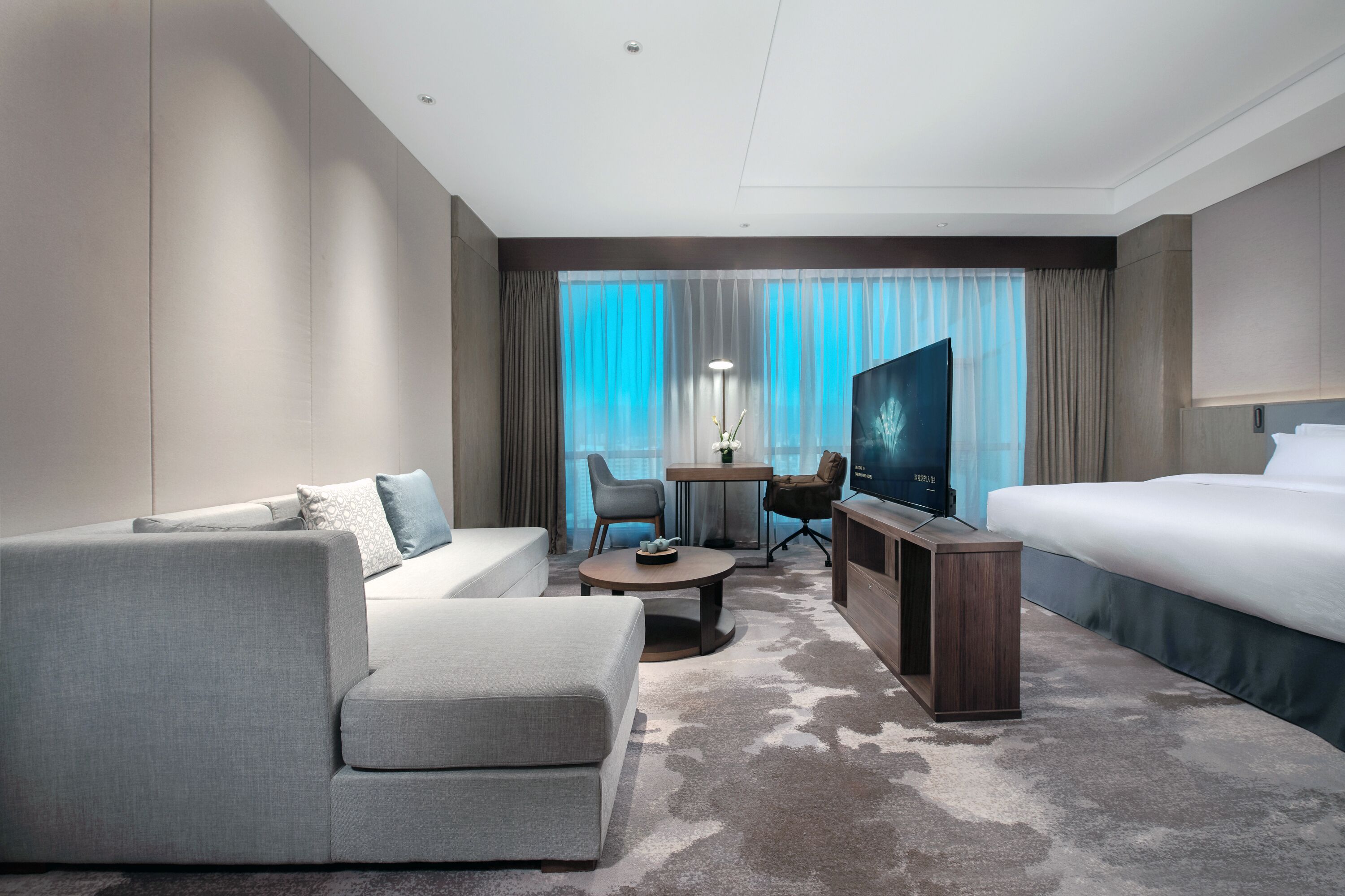 Quarto de hotel moderno com sofá, cama, televisão e uma pequena mesa.