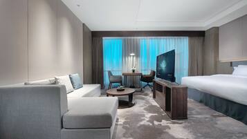 Quarto de hotel moderno com sofá, cama, televisão e uma pequena mesa.