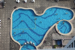Uma grande piscina ao ar livre com várias pistas, rodeada por um terraço revestido com áreas de estar.