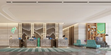 Uma área de recepção de hotel com design moderno, apresentando um balcão de atendimento, dois recepcionistas, uma placa verde e um espaço de estar com um sofá e cadeiras.