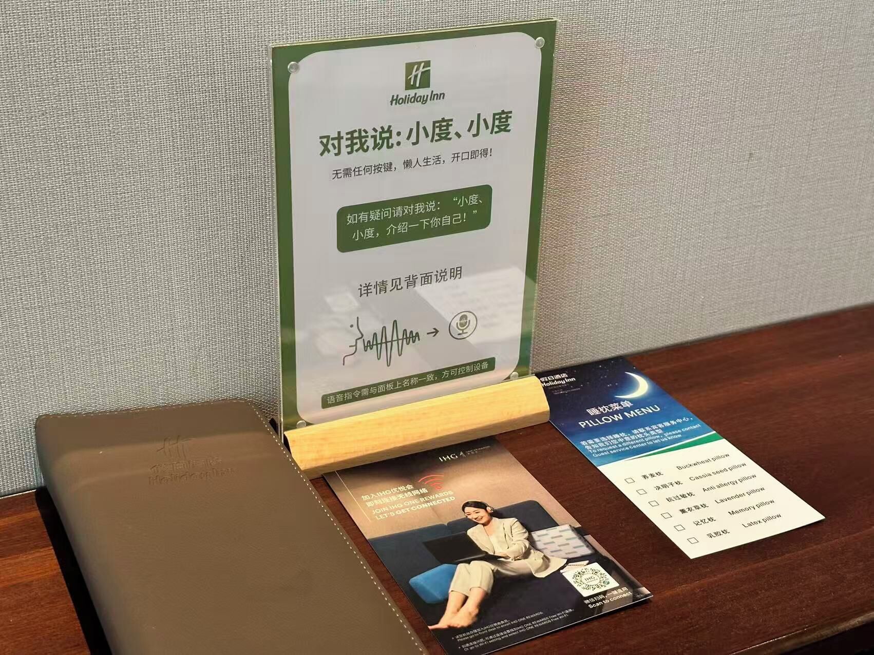 Placa de hotel com mensagem em chinês, cardápio de almofadas e um folheto sobre uma mesa de madeira.