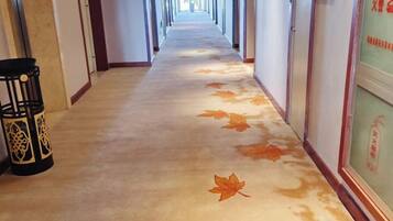 Corredor de hotel com carpete decorado com folhas de outono, uma lixeira e um quadro na parede.