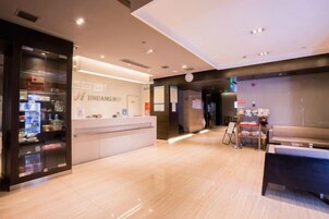 Uma área de recepção de hotel com balcão, sala de espera com sofá e uma vitrine de vidro.