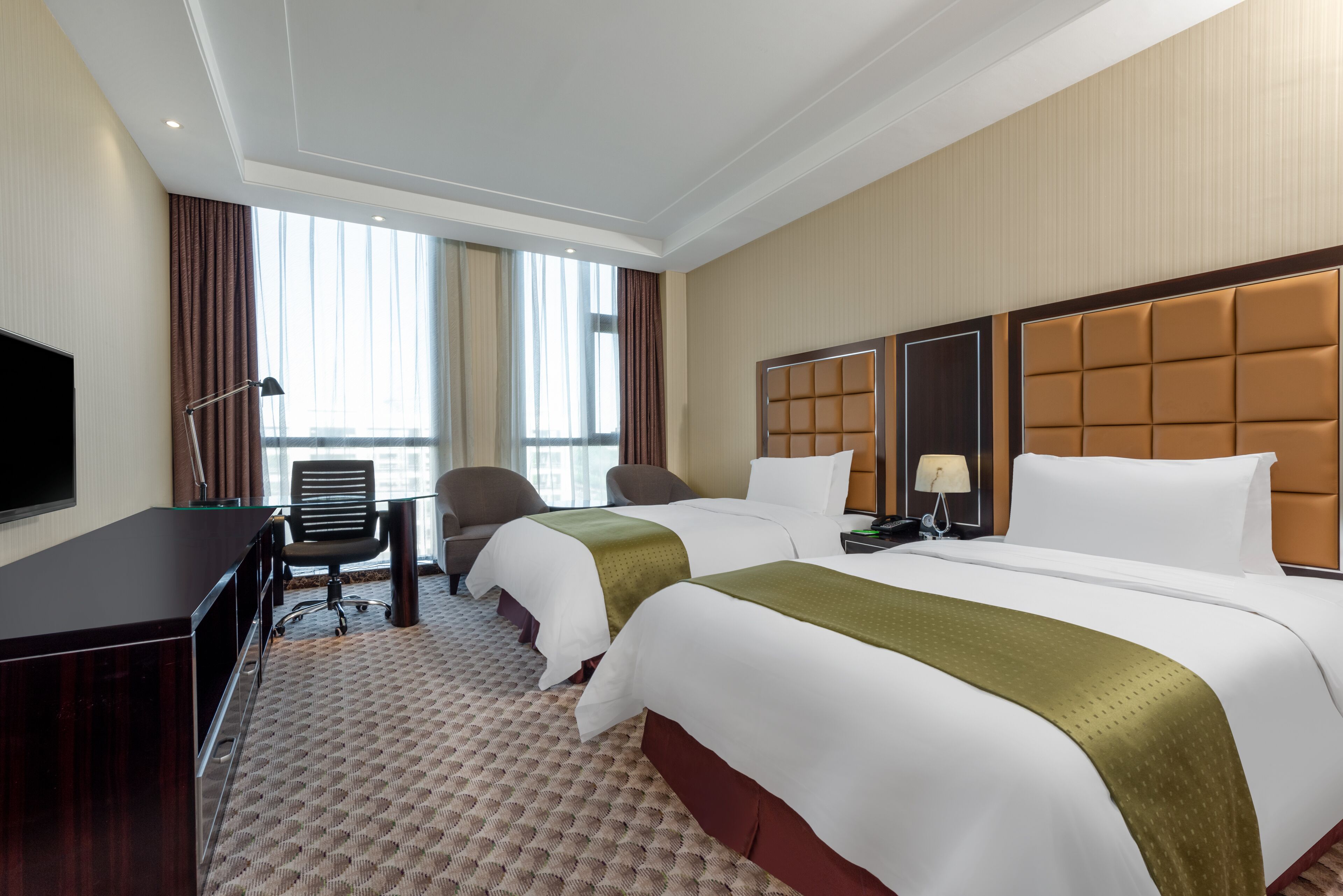 Quarto de hotel com duas camas, uma escrivaninha, uma cadeira e uma televisão.