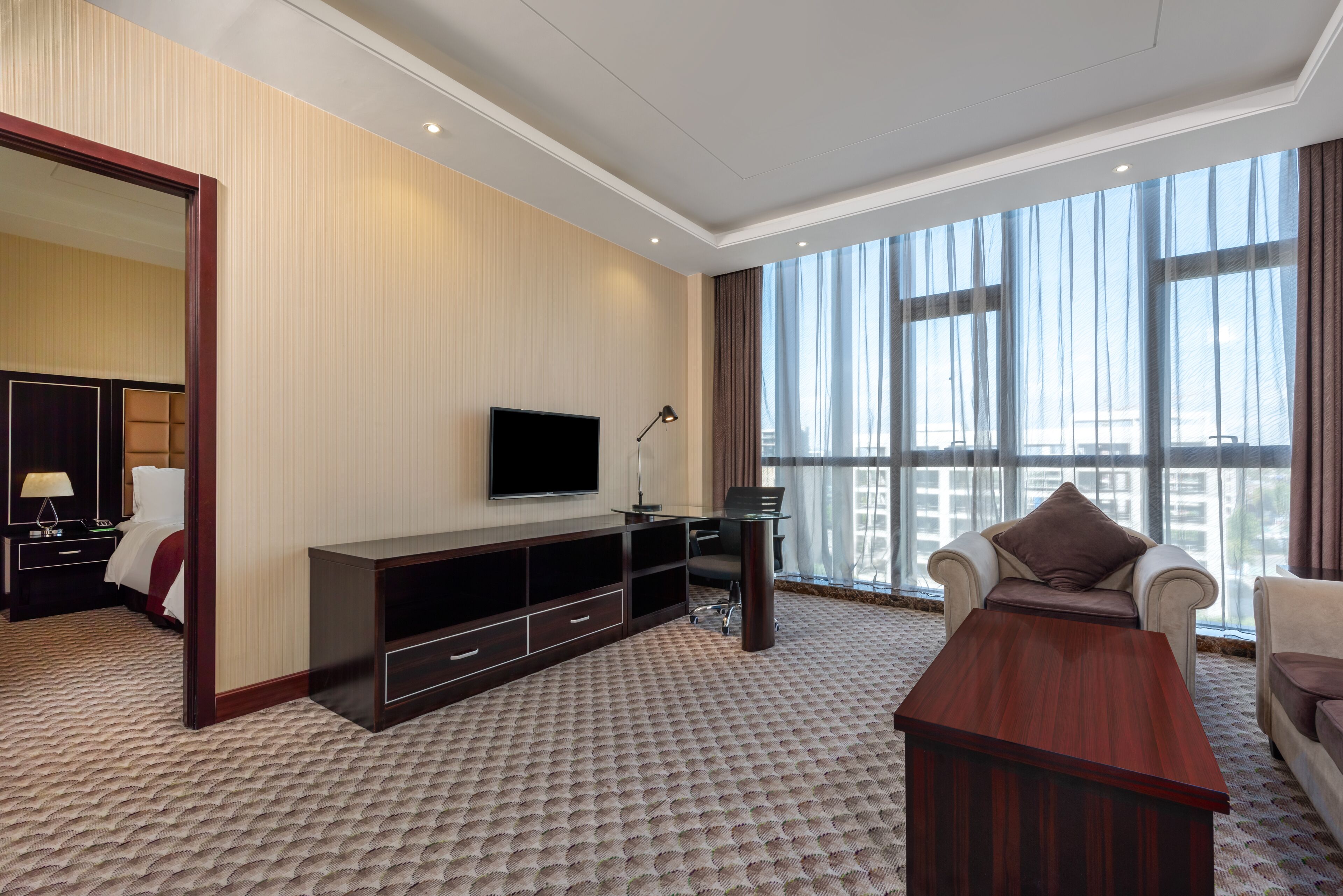 Quarto de hotel com uma janela grande, televisão de tela plana, sofá, mesa de centro e escrivaninha com abajur.