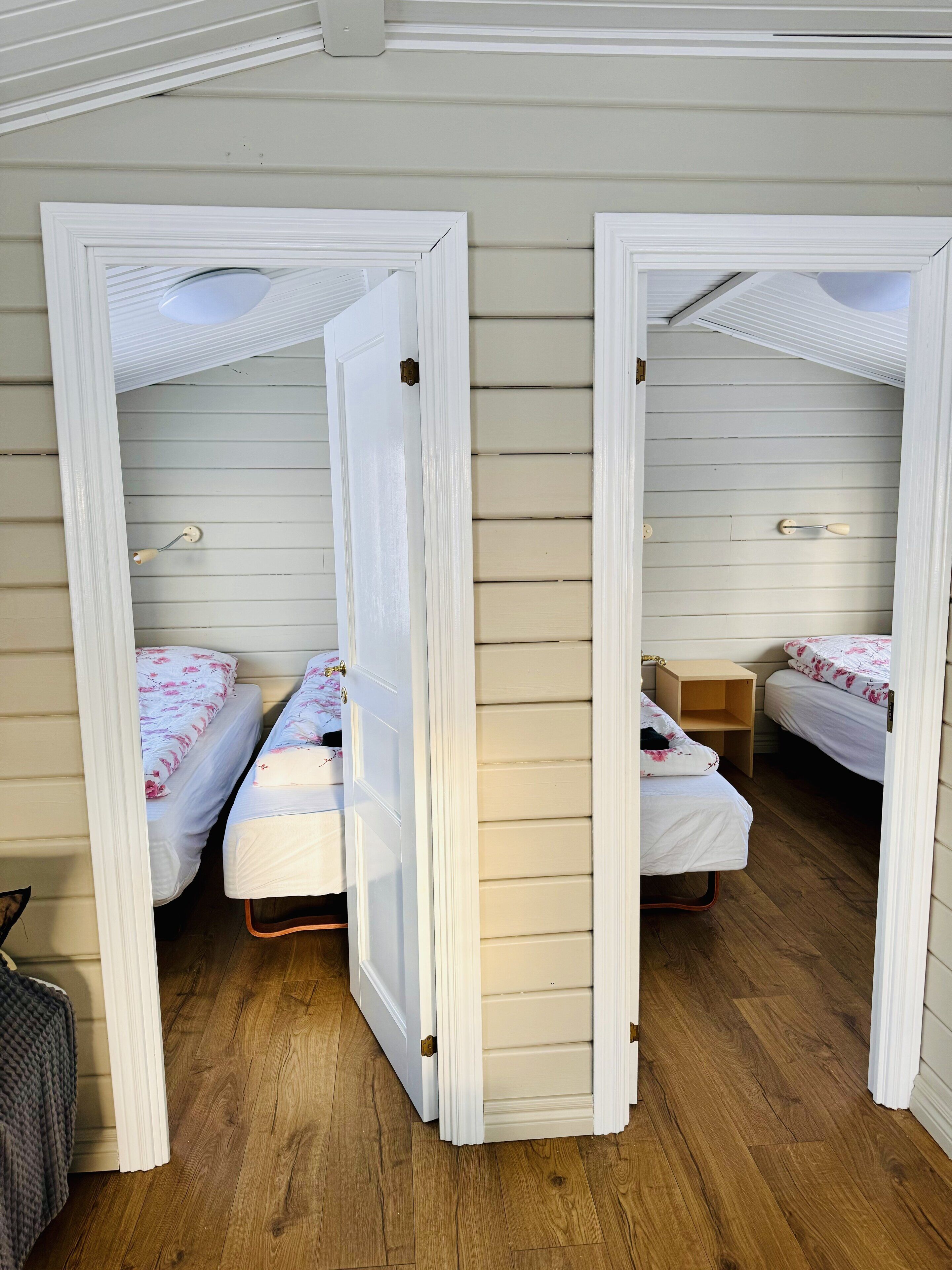 Quarto com duas camas, piso de madeira e porta branca.