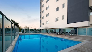 Um hotel moderno com piscina no terraço, guarda-corpos de vidro e espreguiçadeiras.