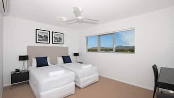 Quarto de hotel com duas camas, um ventilador de teto, janela com vista para a paisagem e uma escrivaninha com cadeira.