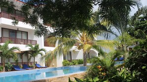 Uma área de piscina com espreguiçadeiras azuis, um muro de pedra e vegetação exuberante.