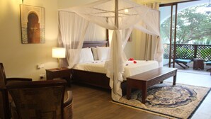 Quarto com cama de dossel, mesa de cabeceira, cadeira e uma grande janela com vista para o verde.