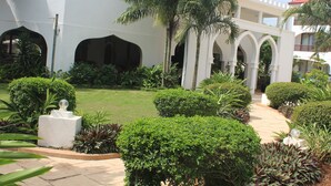 Pátio com um edifício branco, arcos e um caminho central.