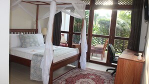 Quarto com cama de dossel, escrivaninha e vista do exterior através de grandes janelas.