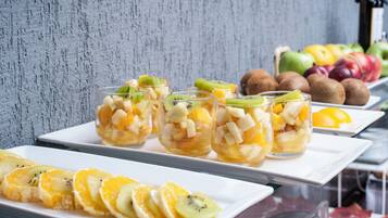 Uma tábua de frutas com laranjas e kiwis fatiados em um prato branco, e uma variedade de frutas inteiras ao fundo.
