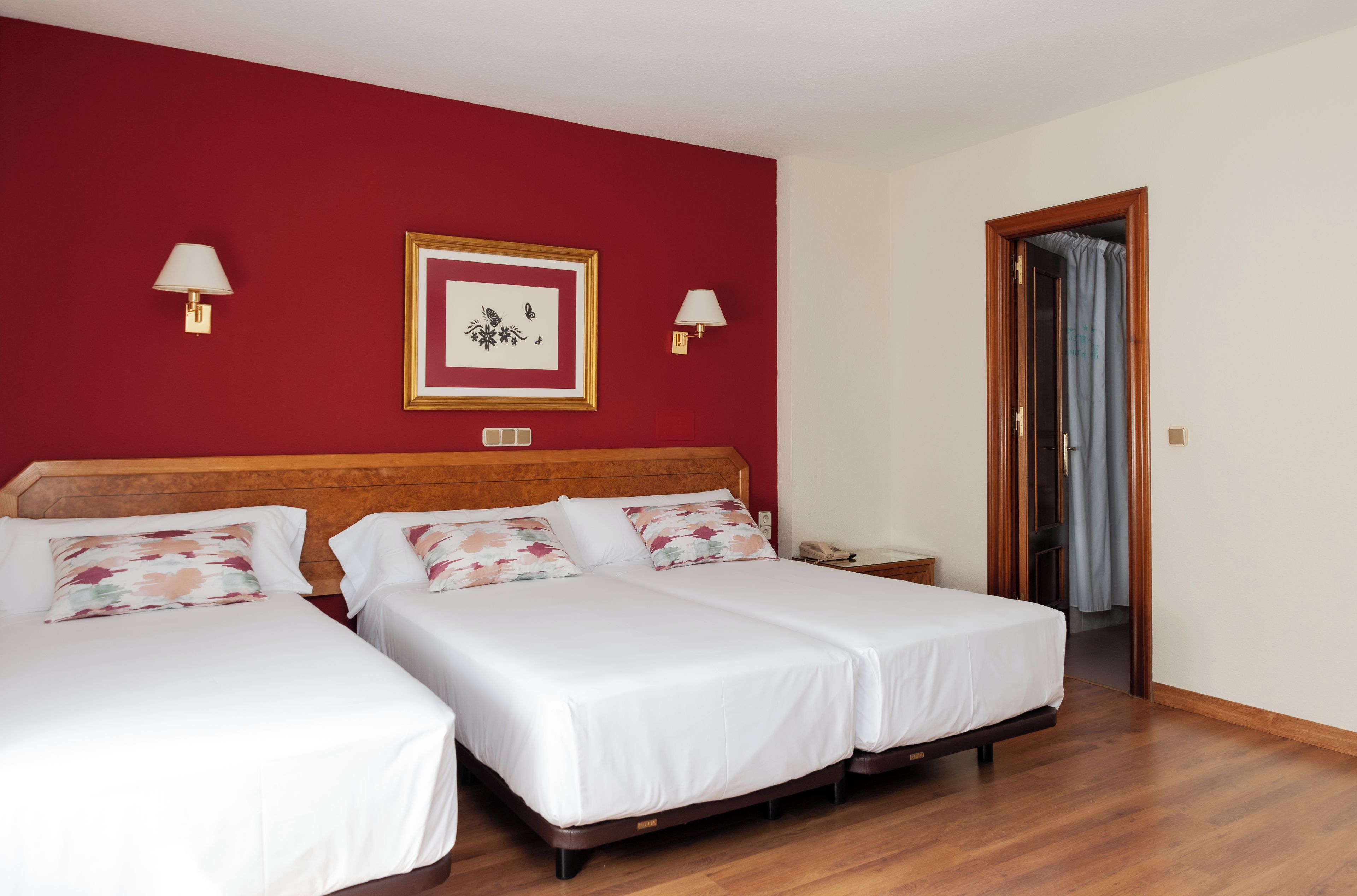 Quarto de hotel com duas camas, cabeceira de madeira, uma obra de arte emoldurada na parede e uma porta com cortina.
