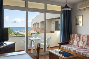 Uma varanda com vista para o mar, um sofá, uma mesa e uma televisão.