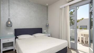 Quarto com cama, mesas de cabeceira, luminária pendente e porta de vidro deslizante que dá para uma área externa.