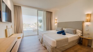 Quarto de hotel com uma cama grande, uma televisão fixada na parede, uma mesinha de cabeceira e uma varanda com cortinas.