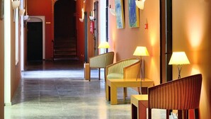 Um saguão de hotel com um corredor extenso, área de descanso com luminárias e obras de arte nas paredes.