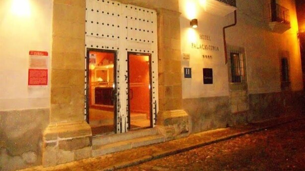 Entrada de hotel com portas duplas, placa indicando saída de incêndio e varanda com grade.