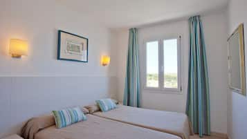 Quarto de hotel com duas camas, janela com cortinas, luminárias fixadas na parede e um quadro emoldurado.