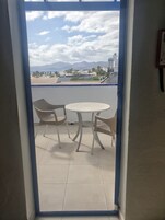 Uma varanda com uma mesa branca e quatro cadeiras, com vista para um horizonte urbano com montanhas e palmeiras.