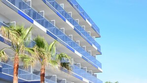 Hotel de vários andares com design moderno, com varandas e palmeiras em primeiro plano.