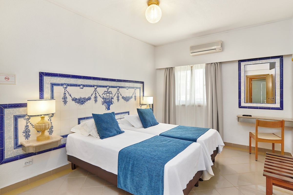 Quarto de hotel com duas camas, uma mesa, uma cadeira e um espelho.