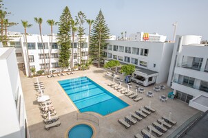 Área de piscina no terraço com espreguiçadeiras e piscina, rodeada por edifícios modernos e palmeiras.