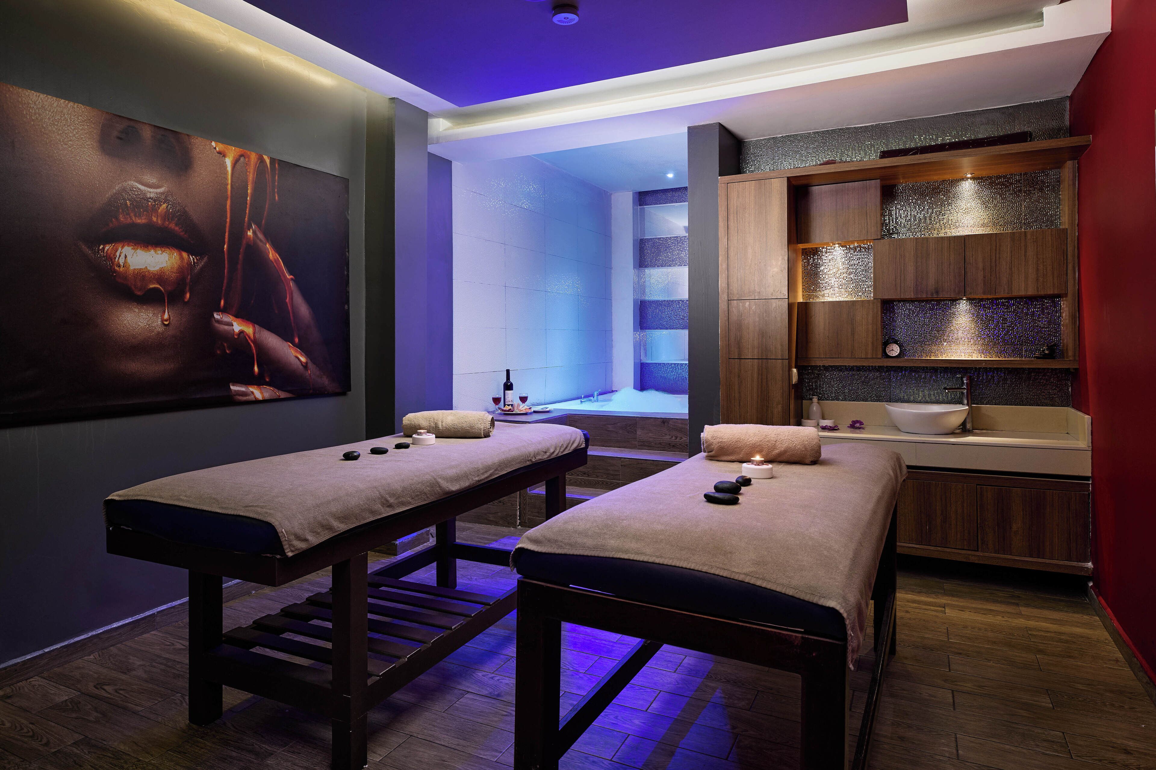 Um espaço de spa com duas mesas de massagem, um cartaz grande na parede e uma prateleira com objetos decorativos.