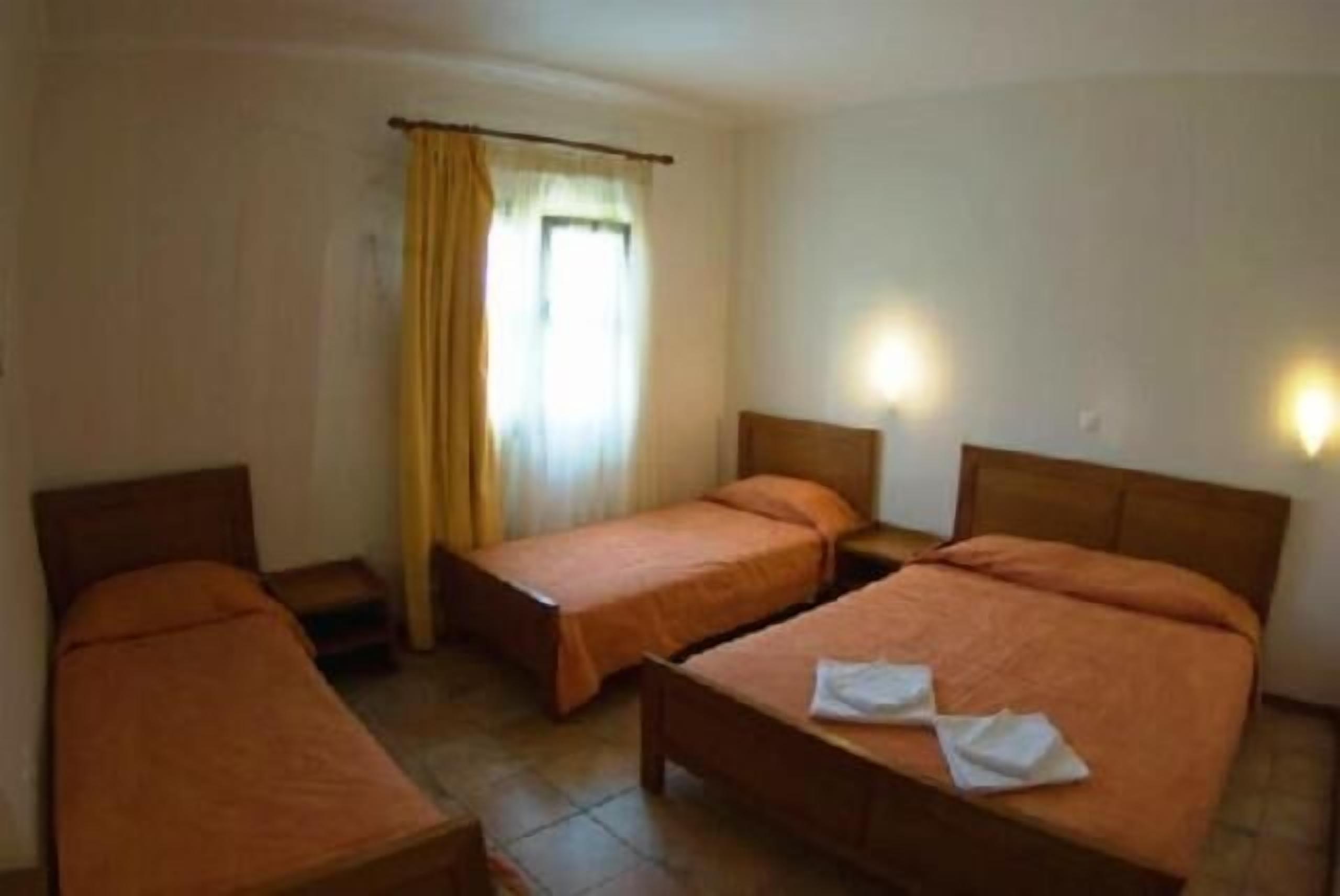 Quarto com três camas de solteiro, uma janela com cortinas amarelas e duas luzes na parede.