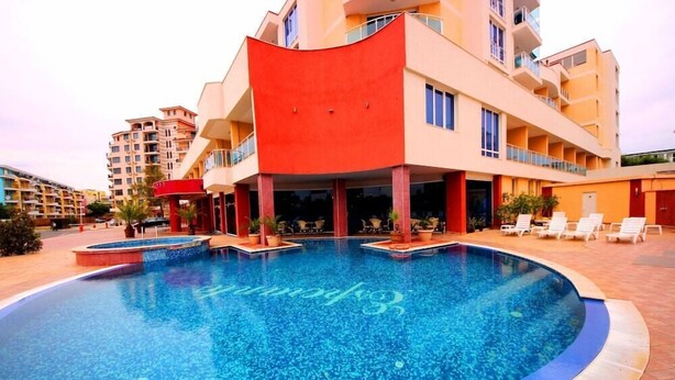 Piscina com borda curva, rodeada por um edifício com varandas e um toldo vermelho.