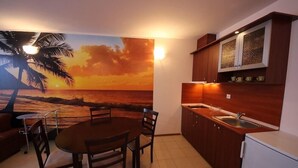 Uma cozinha compacta com área de refeições, um mural na parede com pôr do sol e armários de madeira.