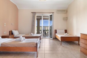 Quarto de hotel com duas camas, porta de correr de vidro para a varanda, cômoda de madeira e ventilador de teto.
