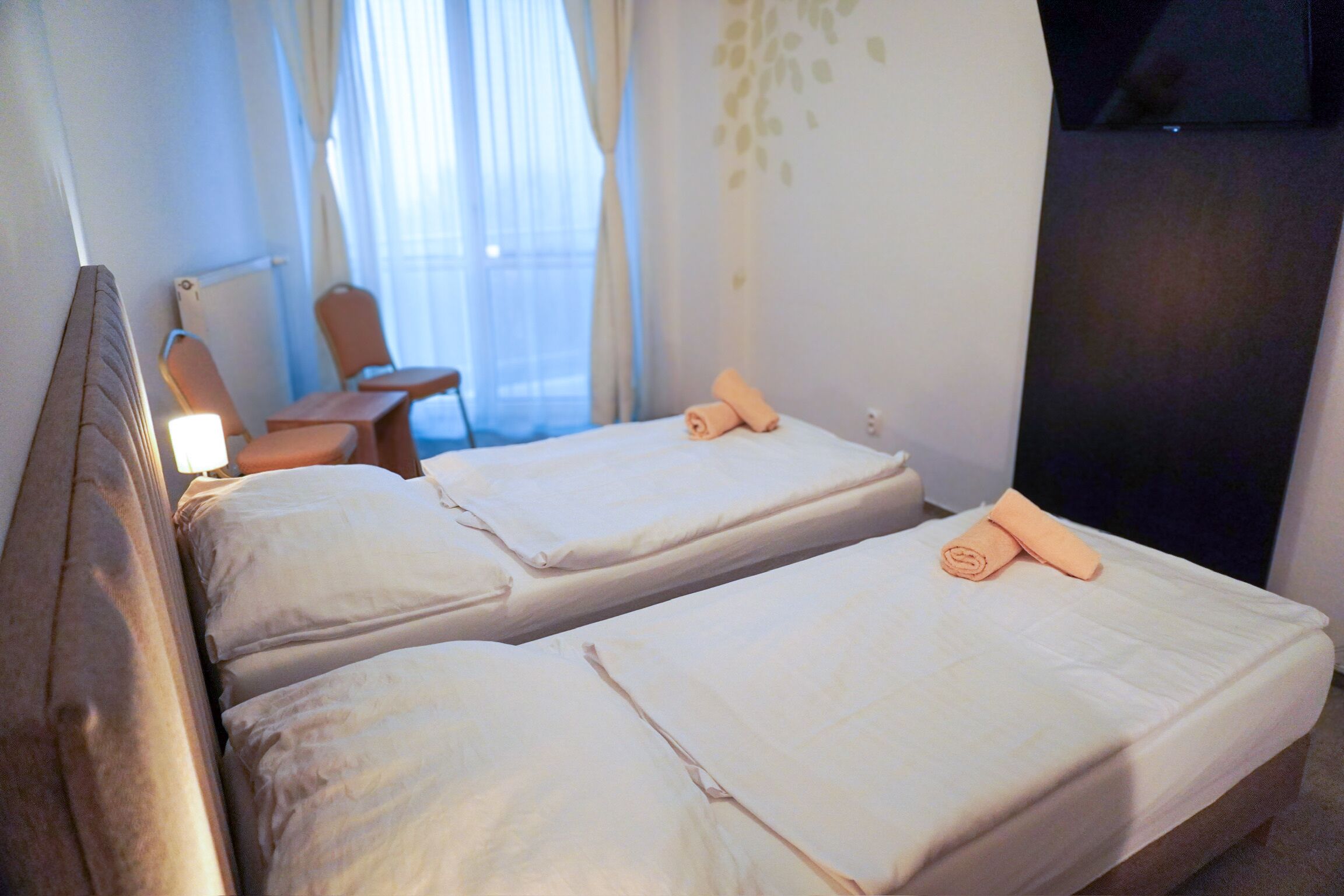 Quarto de hotel com duas camas, uma escrivaninha e uma cadeira.