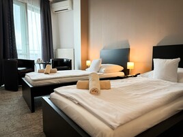 Quarto de hotel com duas camas, uma escrivaninha, uma cadeira e um abajur.