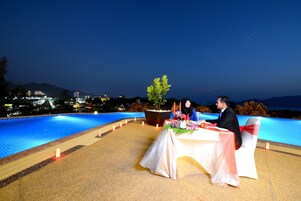 Mesa de jantar montada ao ar livre, com piscina ao fundo.