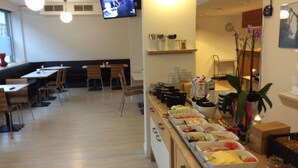 Restaurante com buffet, mesas e cadeiras de madeira, e uma tela de televisão.