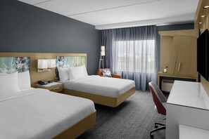 Quarto de hotel com duas camas, uma escrivaninha, uma cadeira, televisão e obras de arte nas paredes.