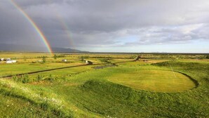 Paisagem rural com arco-íris, campos abertos e alguns edifícios dispersos.