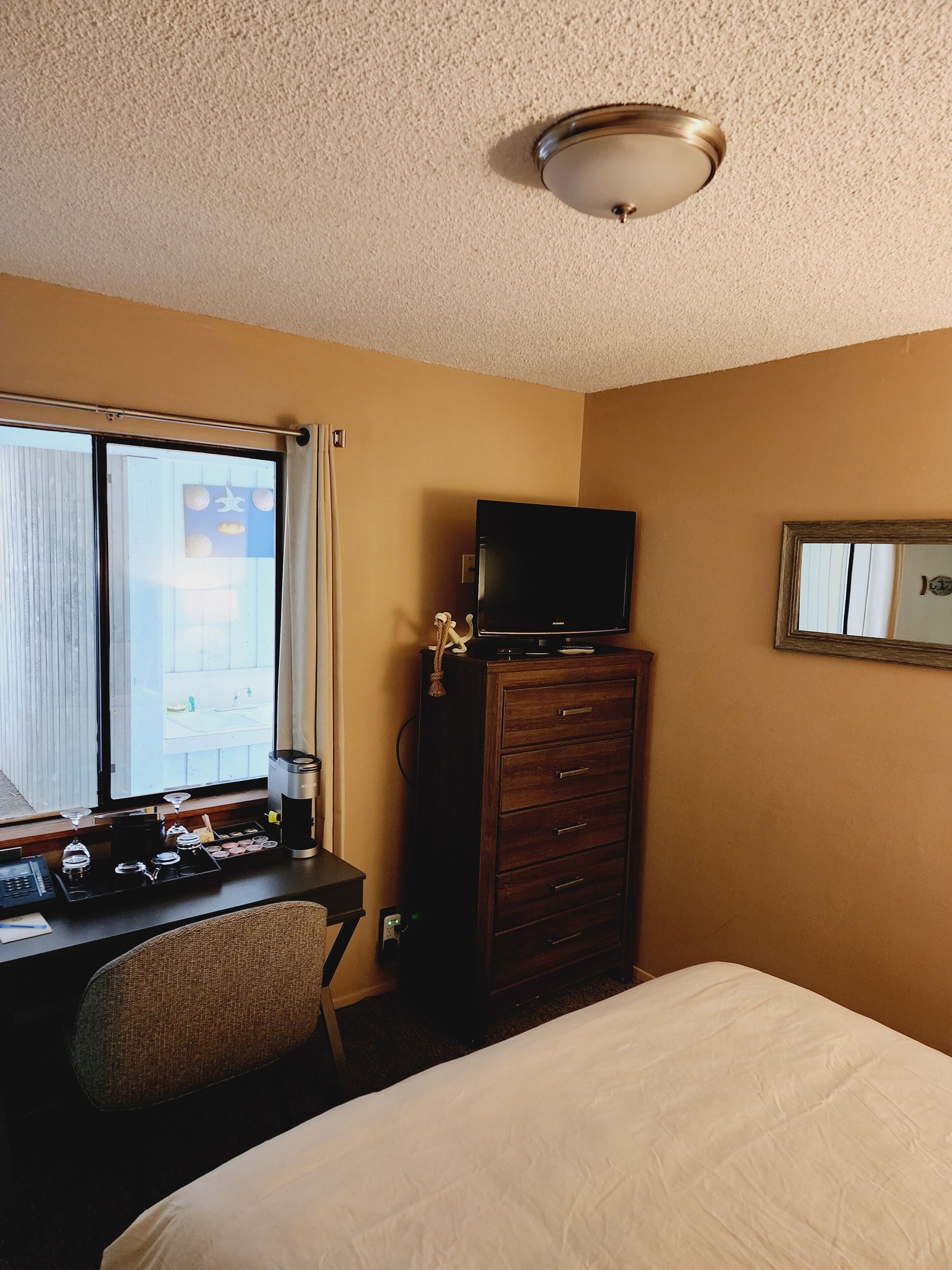 Quarto de hotel com cama, escrivaninha com computador, cafeteira e televisão em um aparador.