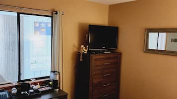 Quarto de hotel com cama, escrivaninha com computador, cafeteira e televisão em um aparador.