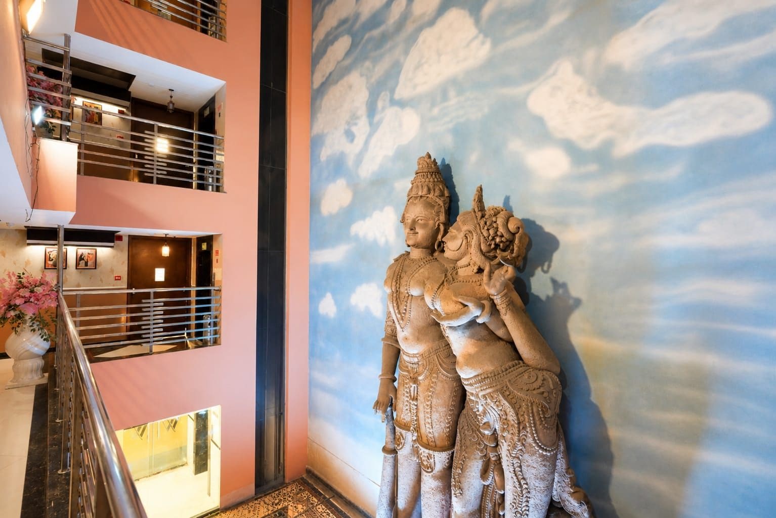 Estátua de uma divindade em um saguão com design de interiores moderno, incluindo uma escadaria e um mural de céu.