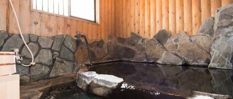 Interior de cabana de madeira com hidromassagem de paredes de pedra e uma janela.