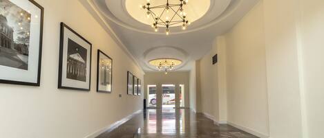 Um corredor com quadros nas paredes, um candelabro e um chão de mármore polido.
