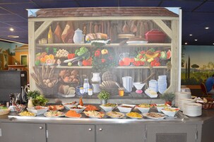 Disposição de buffet com diversos alimentos e utensílios de cozinha expostos em prateleiras e balcões.