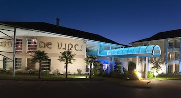 Hotel com design moderno, apresentando uma galeria coberta e palmeiras na frente.