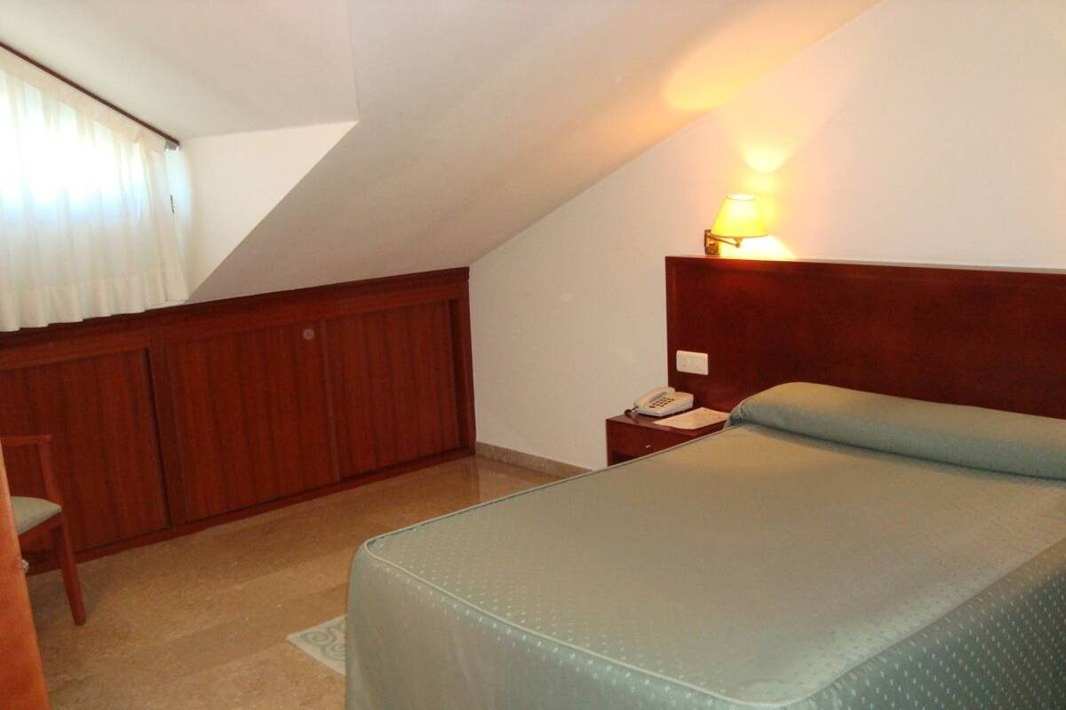 Quarto com cama, mesa de cabeceira, abajur, guarda-roupa de madeira e uma cadeira.