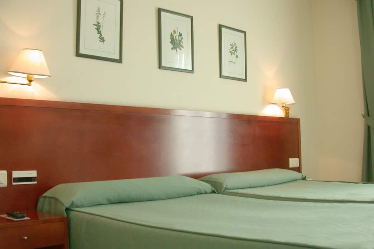 Quarto de hotel com uma cama de casal, duas luminárias de cabeceira e três gravuras de plantas emolduradas na parede.
